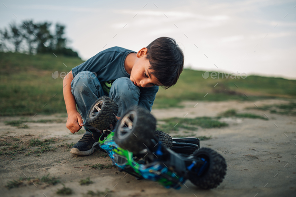 Sad boy looking at his overturned and broken toy car outdoors. Stock Photo by zamrznutitonovi